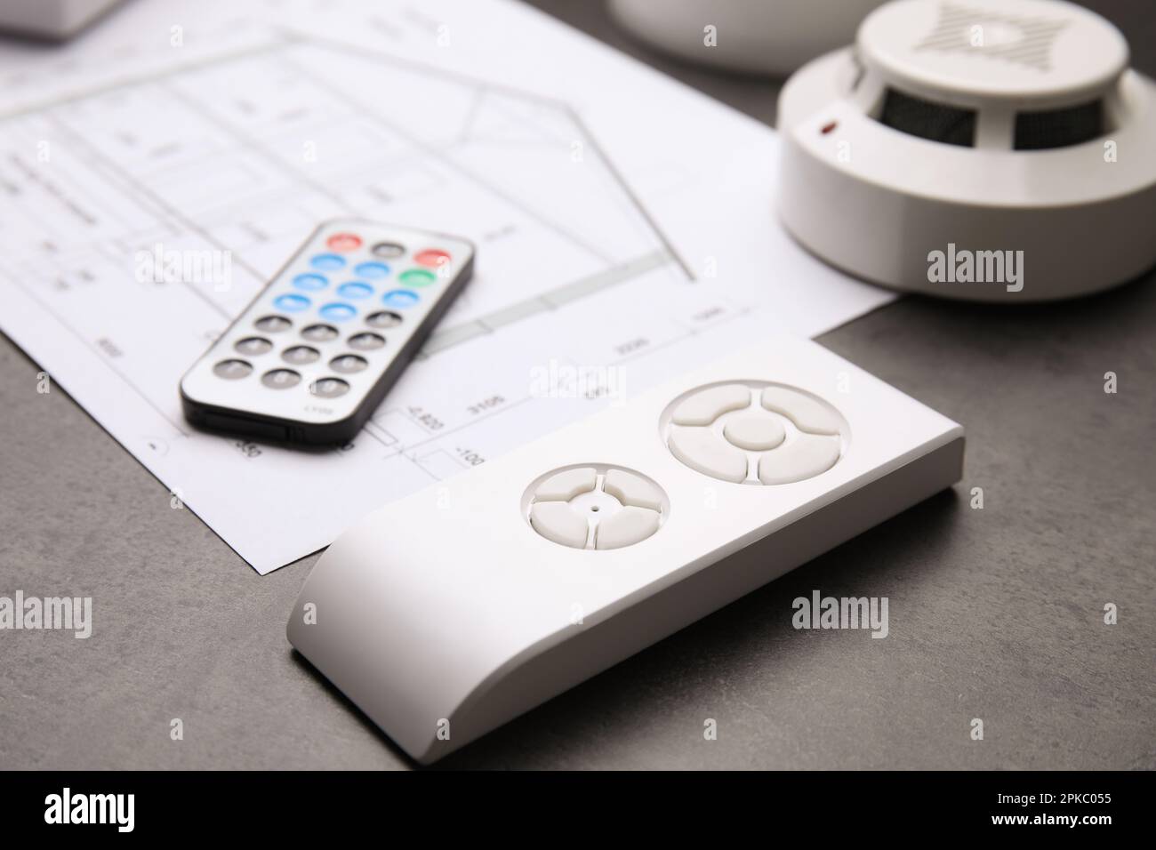Remote controls, smoke detector and building plan on grey table ...