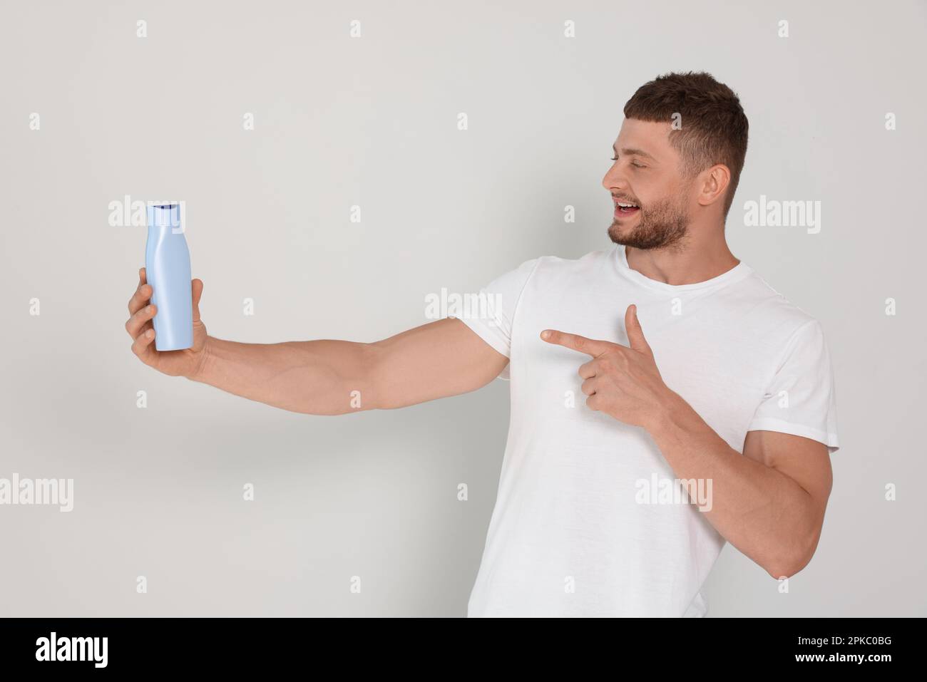 Handsome young man holding bottle of shampoo on white background Stock ...