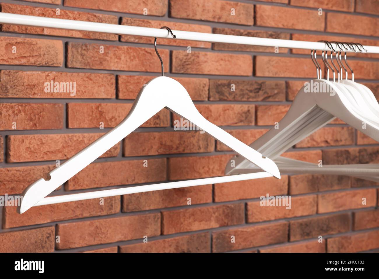 White clothes hangers on rail near red brick wall Stock Photo - Alamy