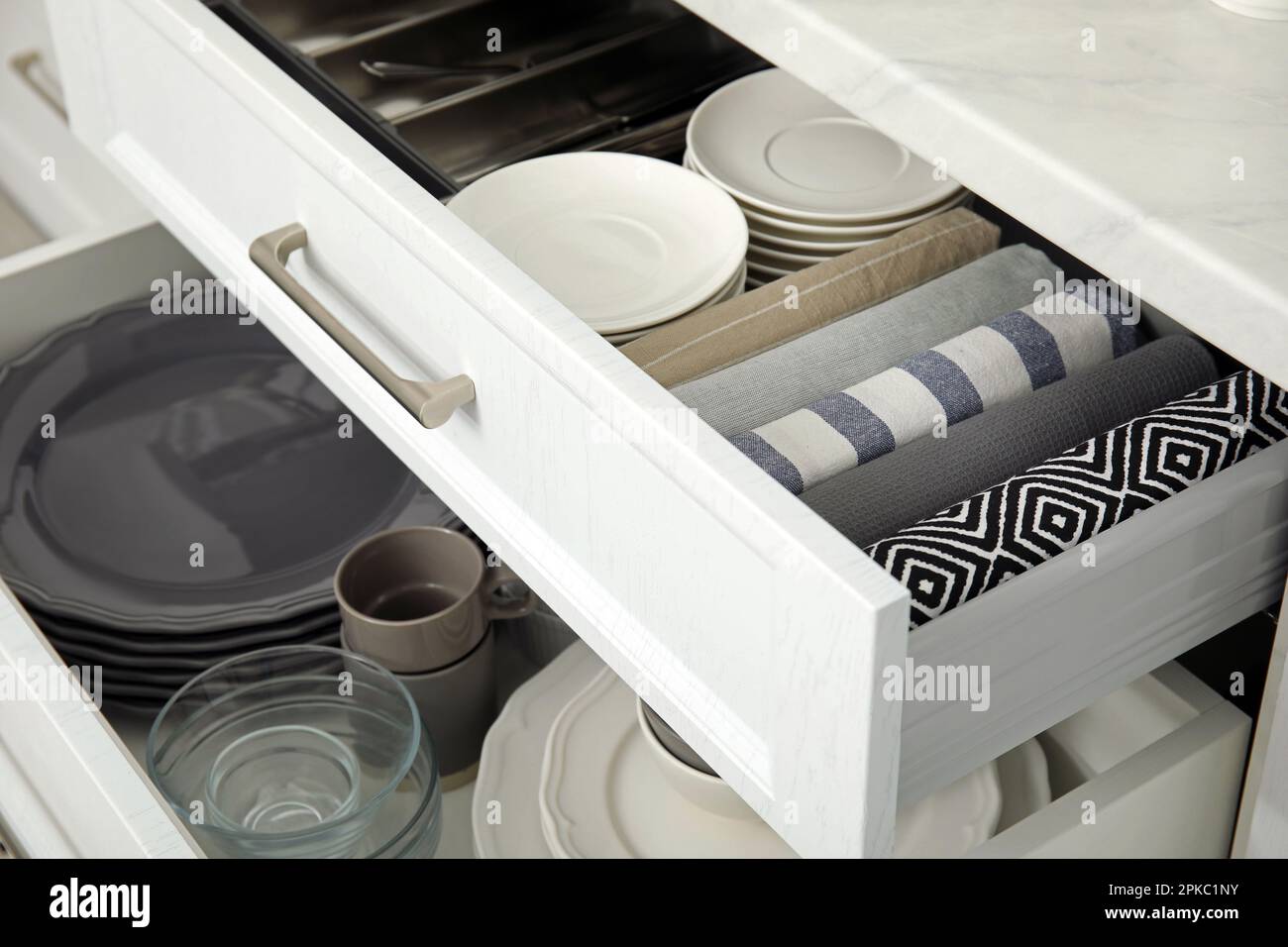 Open drawers of kitchen cabinet with different dishware and towels ...