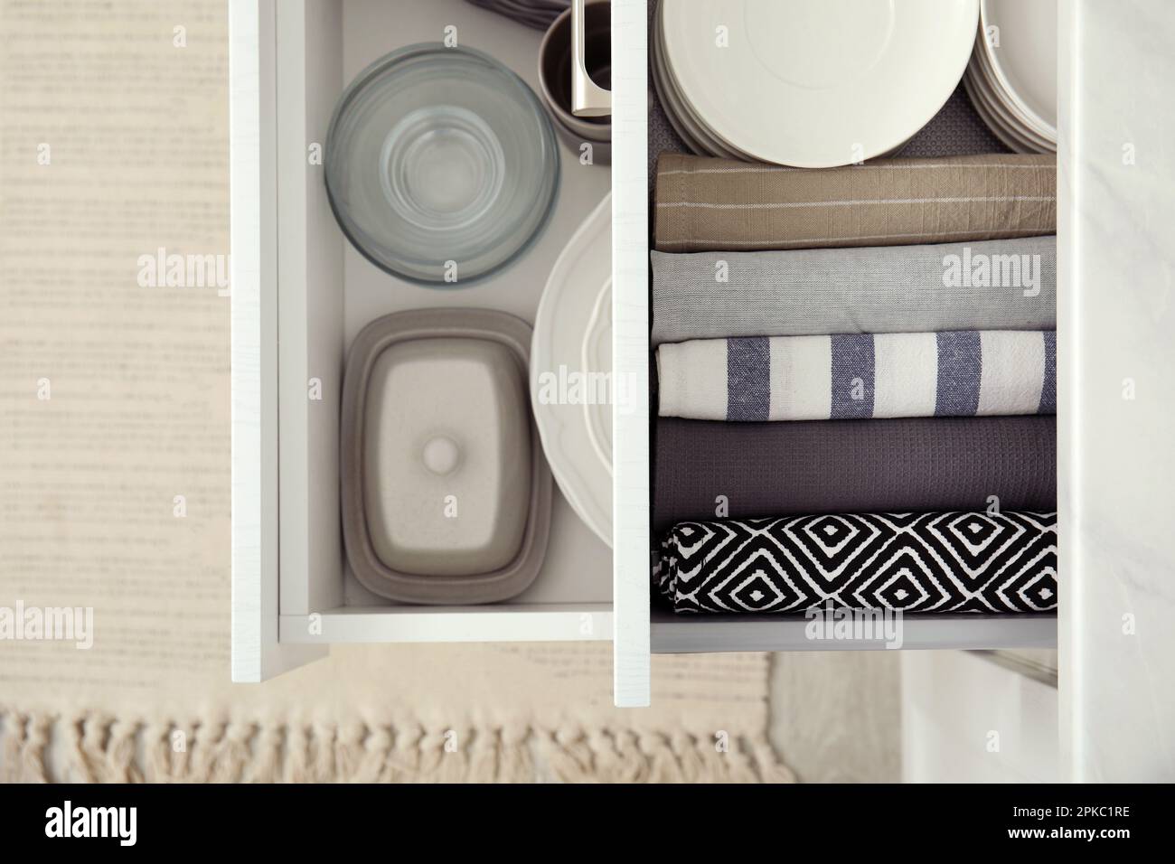 Open drawers of kitchen cabinet with different dishware and towels, top ...