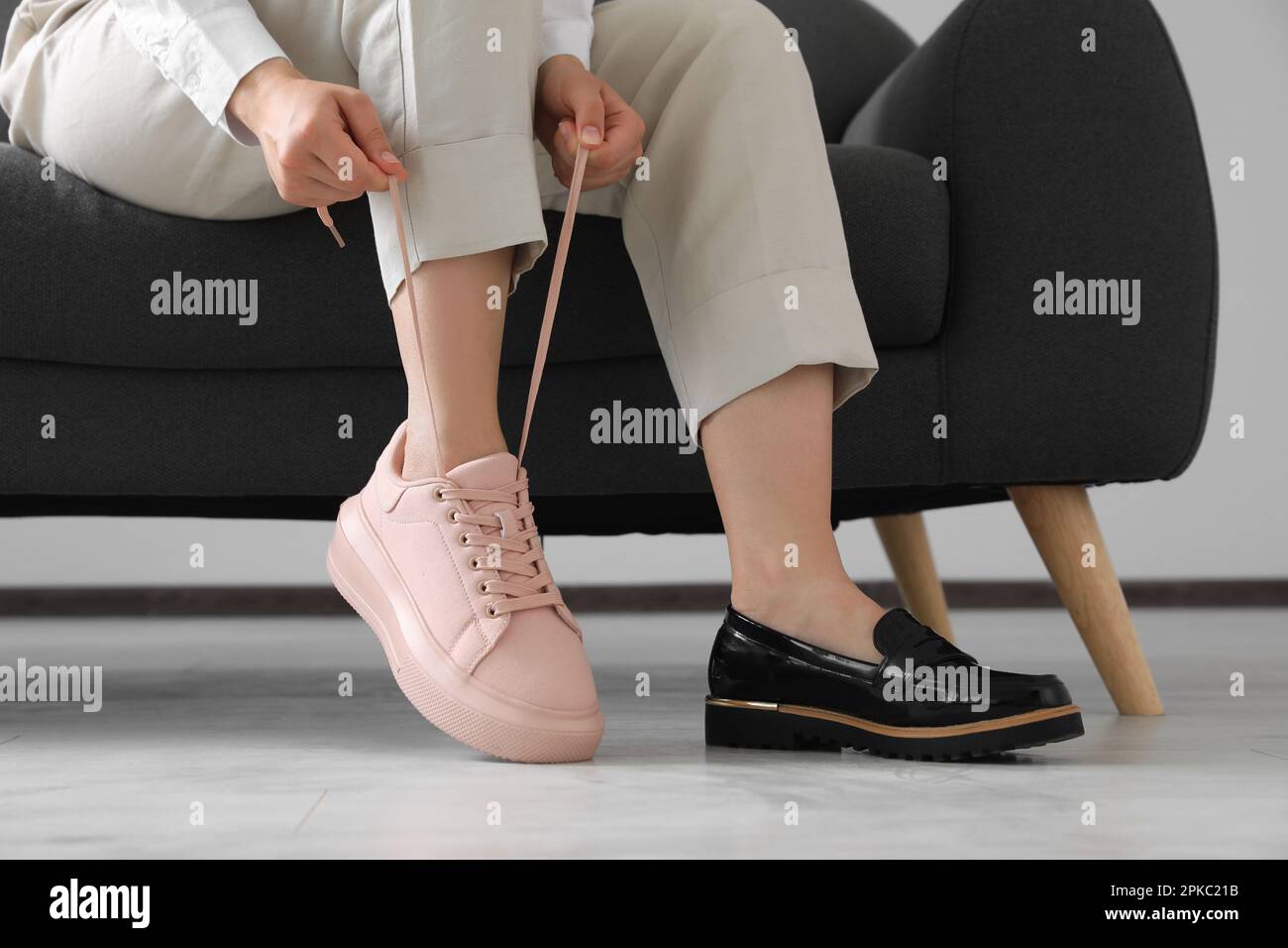 Woman taking off uncomfortable shoes and putting on sneakers in office ...
