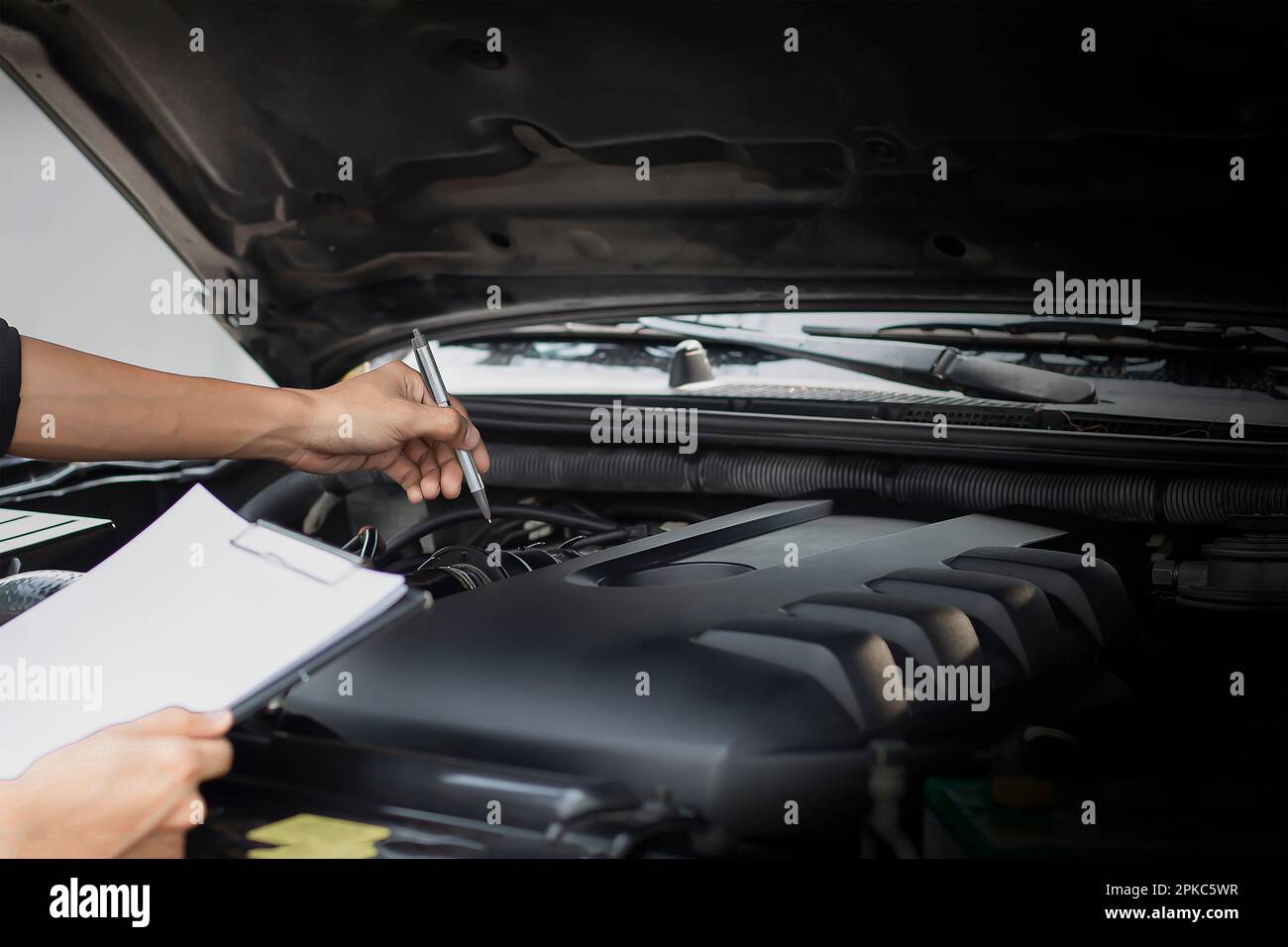 Automobile mechanic repairman checking a car engine with inspecting writing to the clipboard the ...