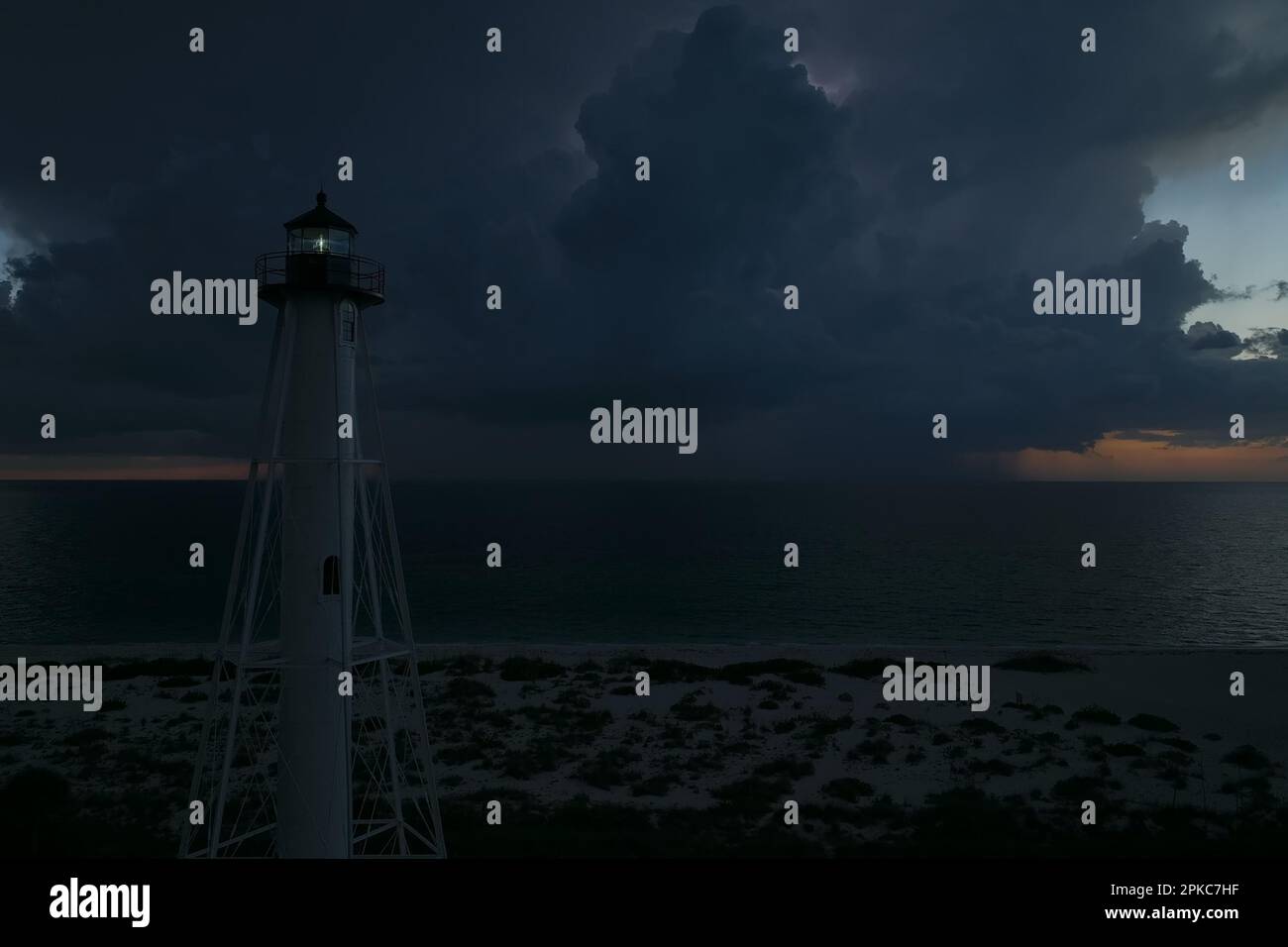White tall lighthouse on sea shore with blinking light at stormy night ...