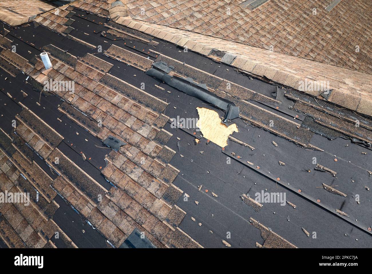 Wind damaged house roof with missing asphalt shingles after hurricane ...
