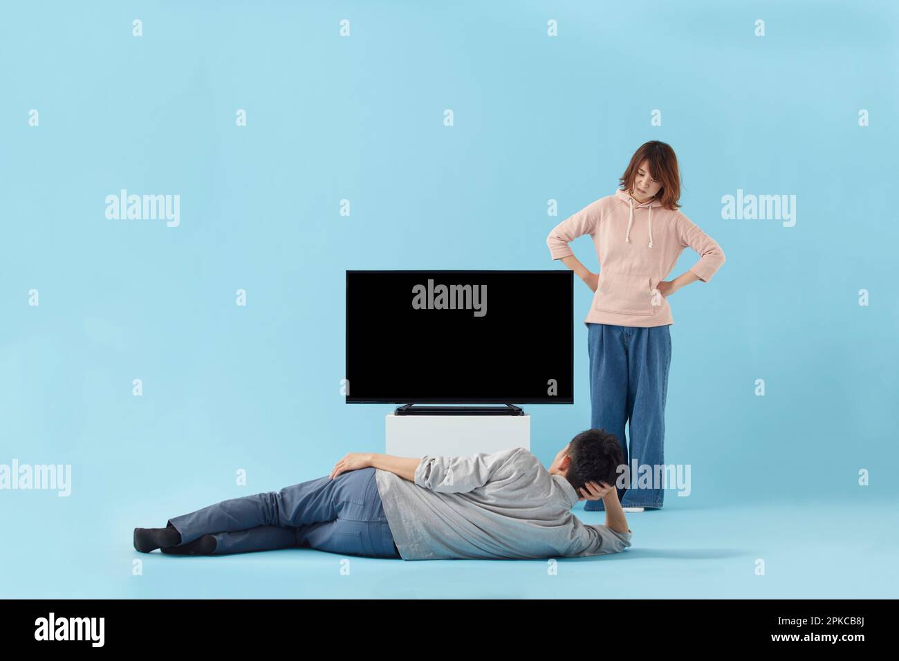 Woman frustrated by man lying down in front of TV Stock Photo - Alamy