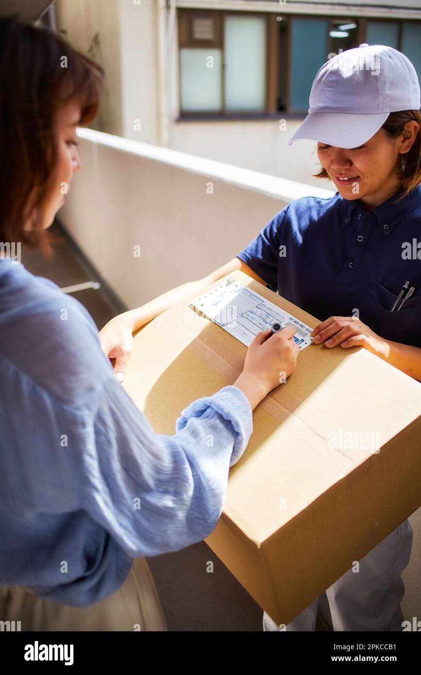 Woman in work clothes handing a cardboard box at the entrance and a ...