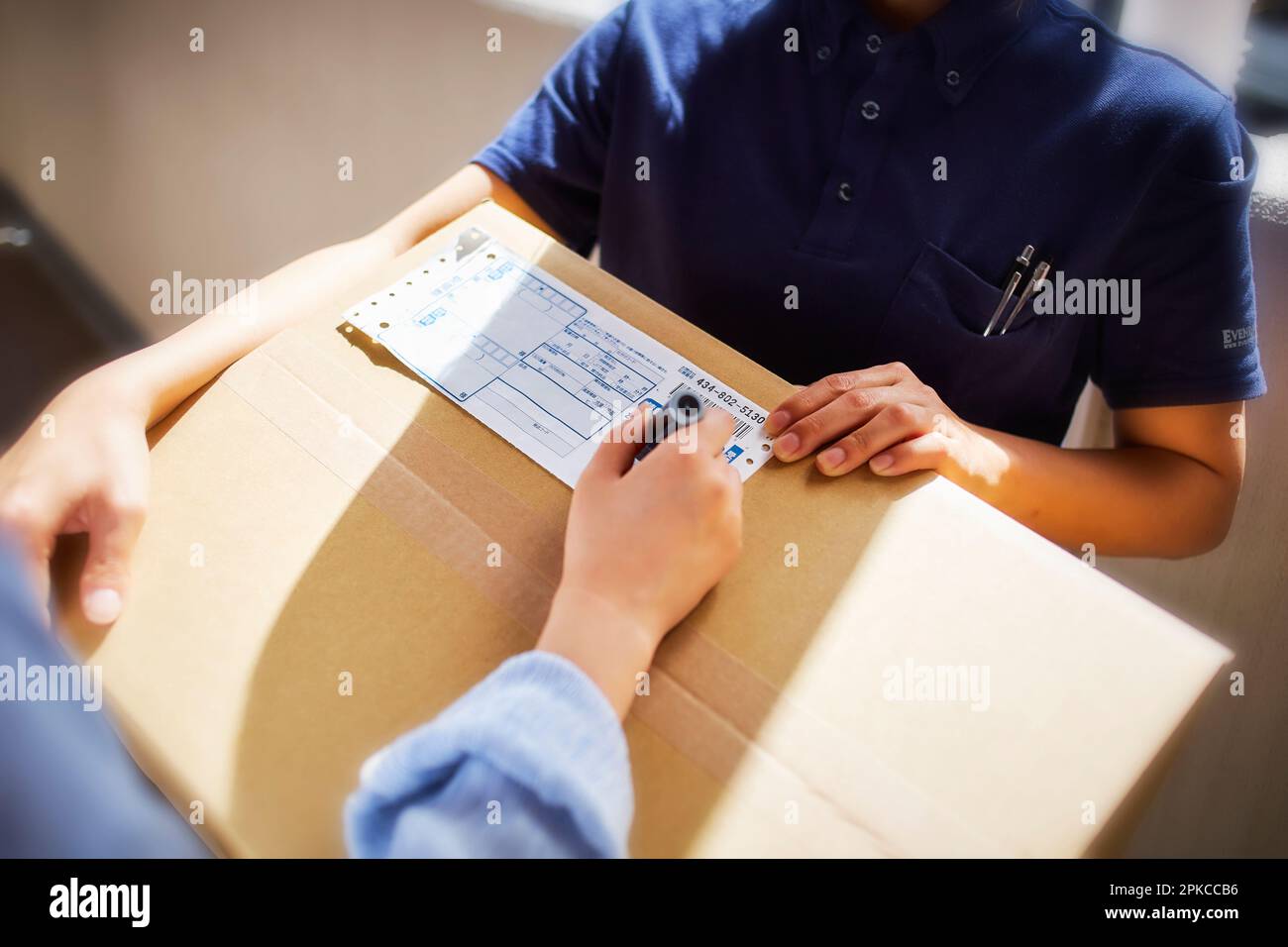 Man in work clothes handing a cardboard box at the entrance and woman ...