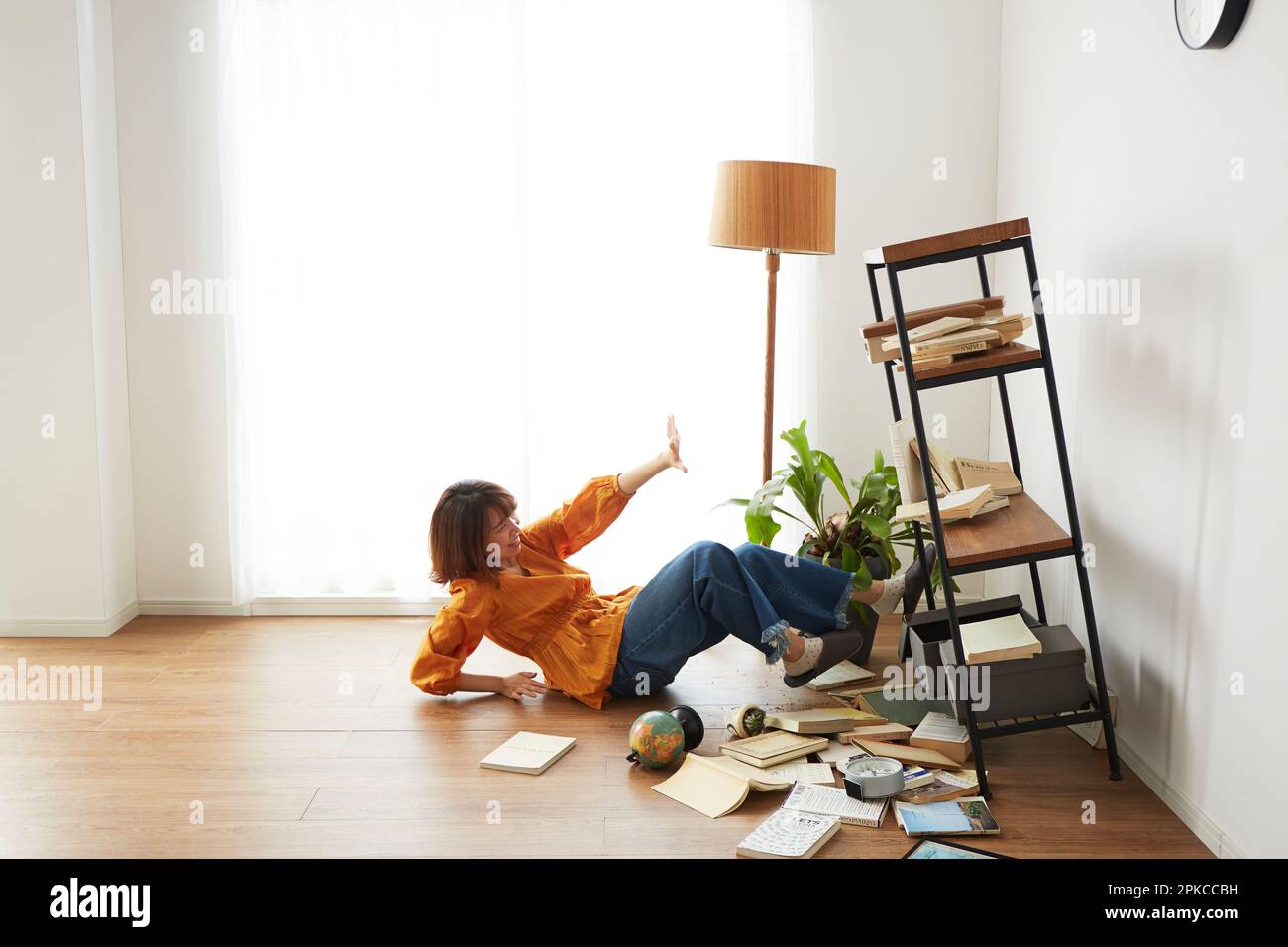 Surprised woman next to a bookcase that fell over during an earthquake ...