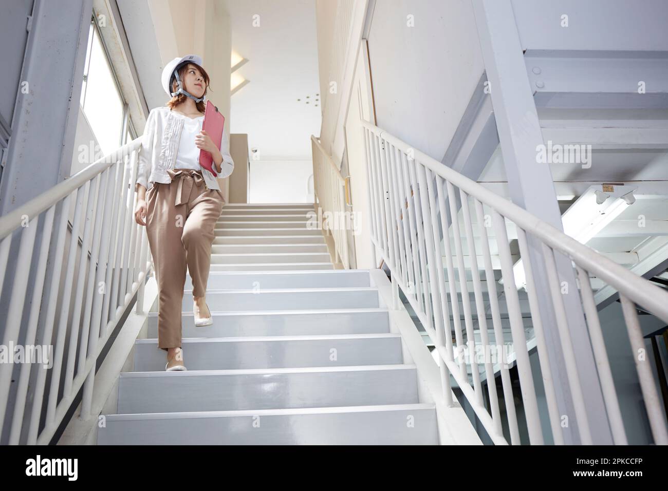 Woman wearing a helmet and carrying documents while descending a flight of stairs Stock Photo ...