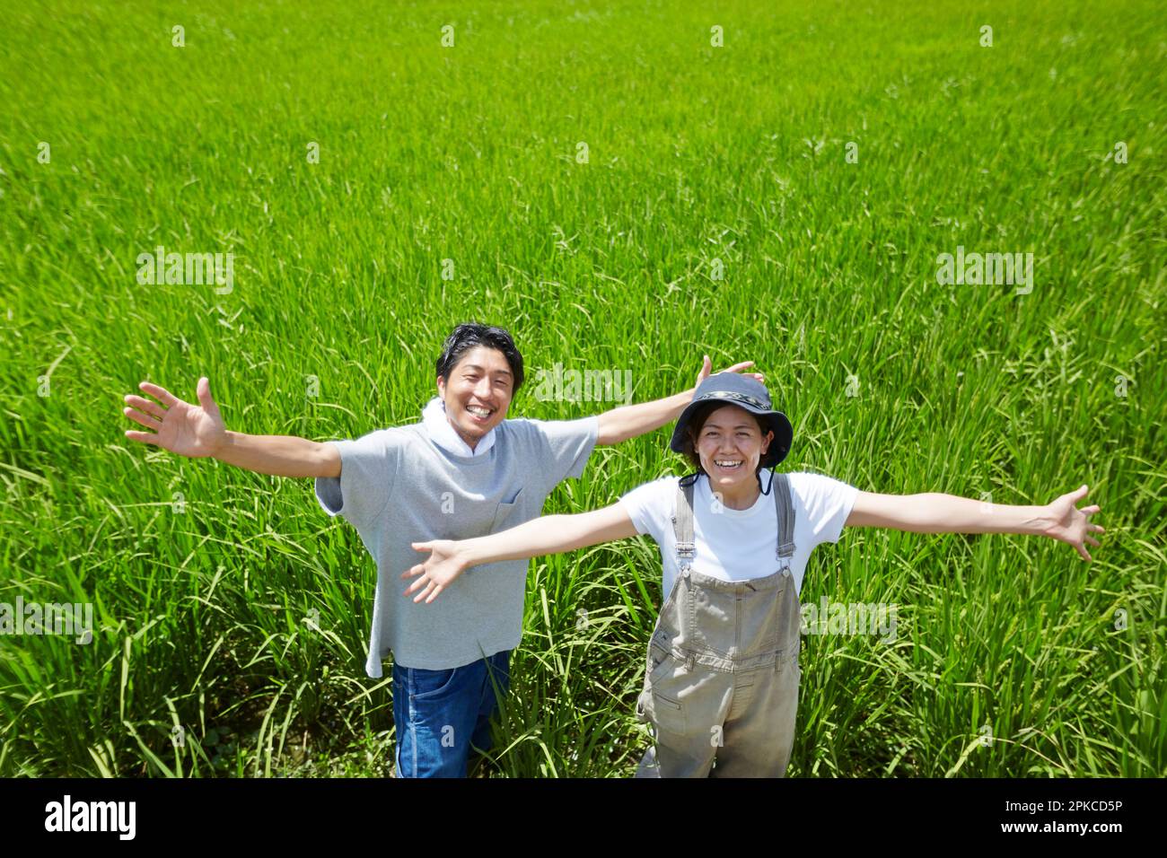 Smiling man and woman with arms outstretched in front of paddy field ...