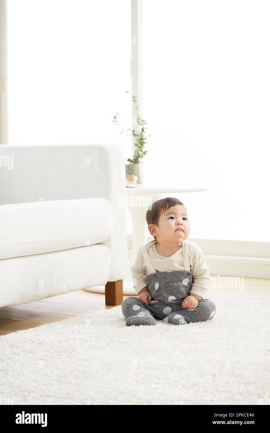 Baby sitting on white rug Stock Photo - Alamy