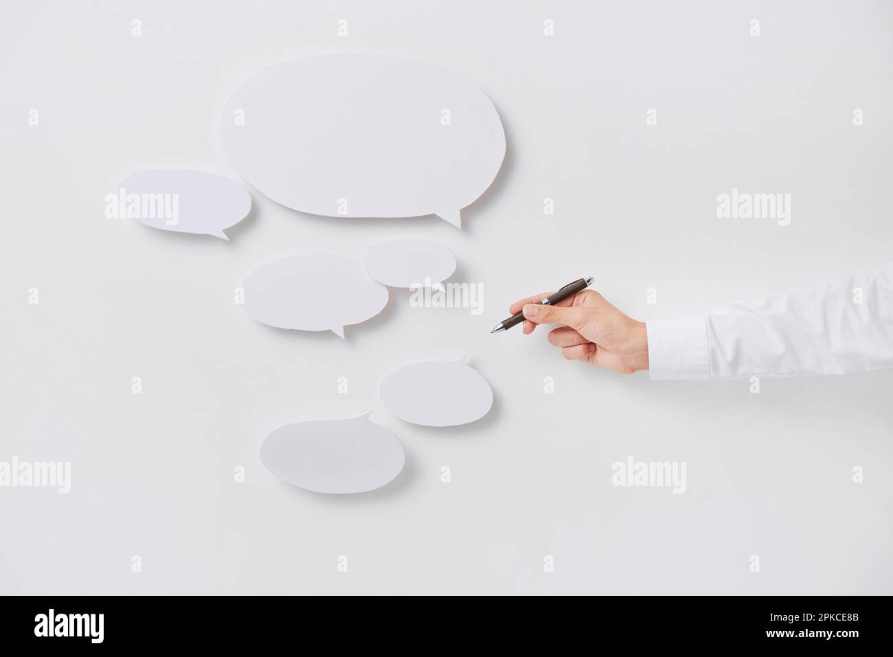 Multiple speech balloons and a person's hand with a pen Stock Photo - Alamy