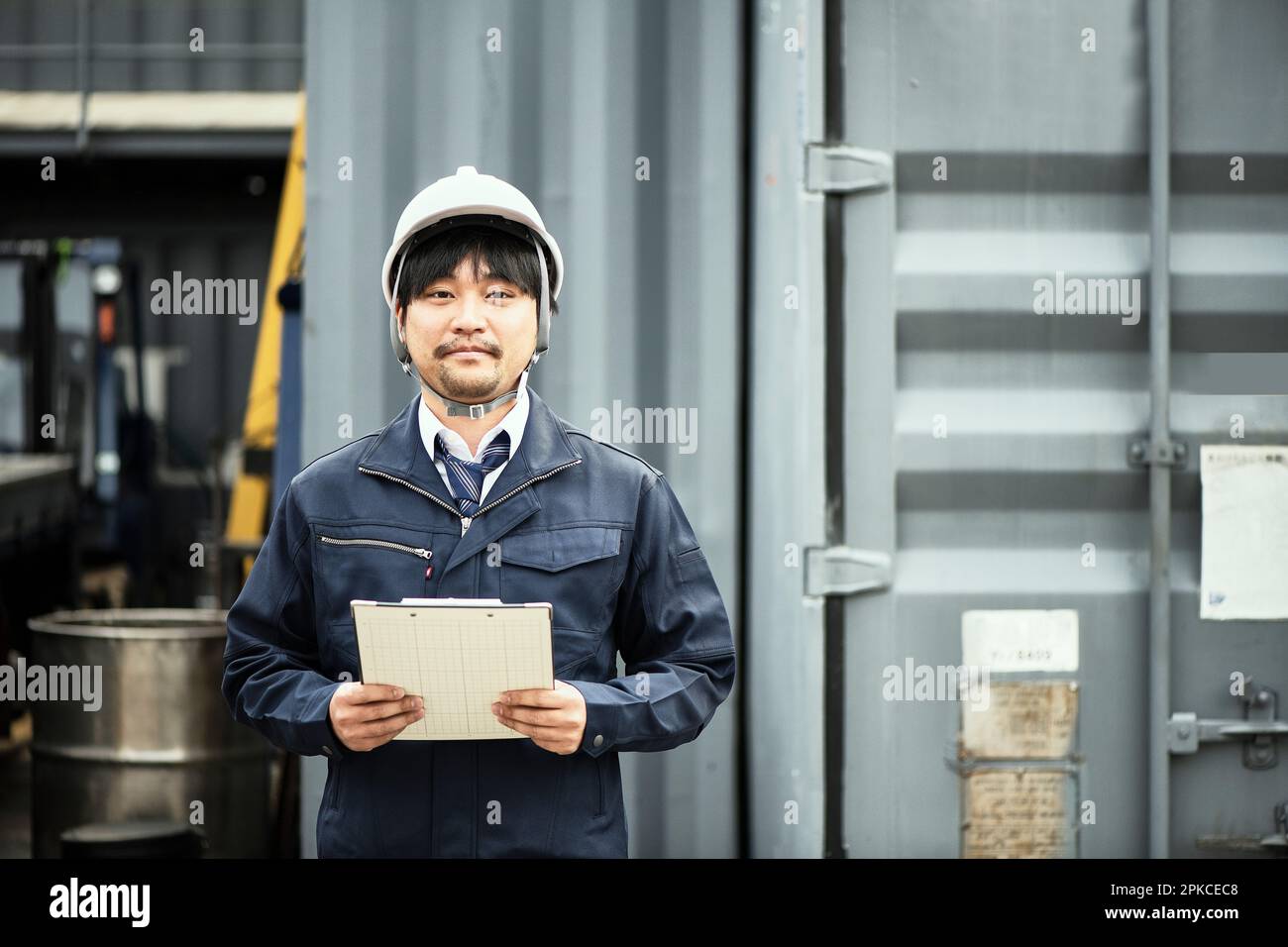 Man in work clothes and helmet standing with container in background ...