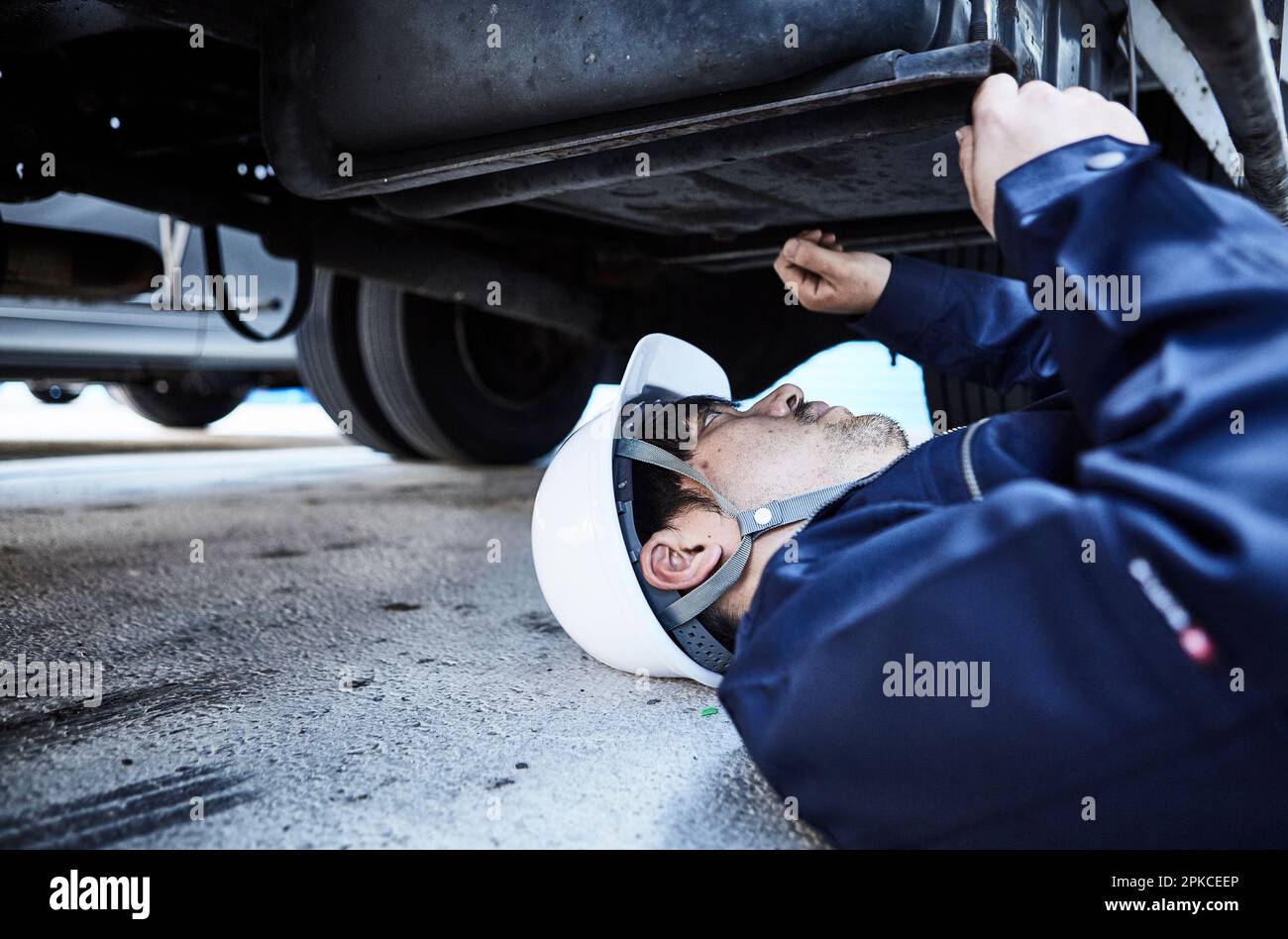 Man in work clothes and helmet working under car Stock Photo - Alamy