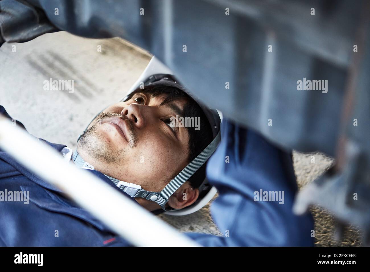 Man in work clothes and helmet working under a car Stock Photo - Alamy
