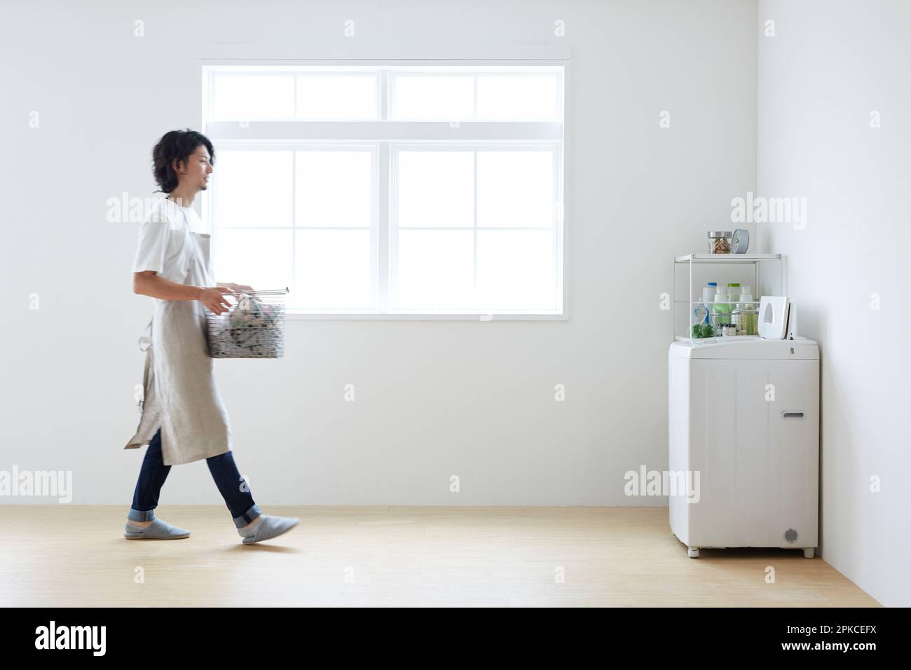 Man carrying laundry to washing machine in simple room Stock Photo - Alamy