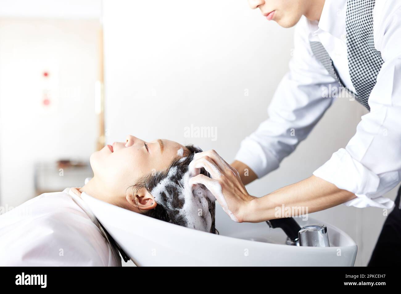 A hairdresser and a customer shampooing their hair on the shampoo table ...