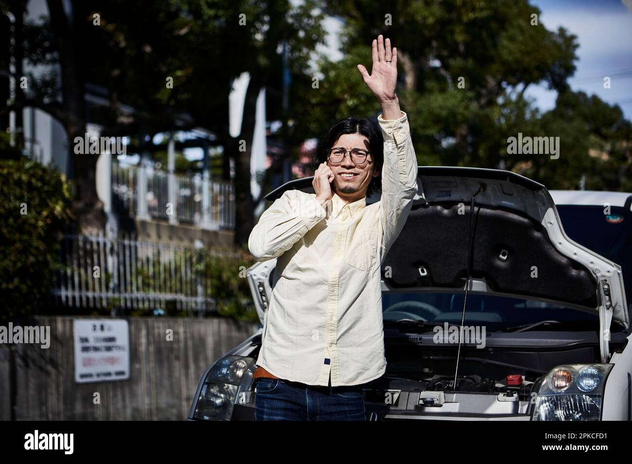 Man raising his hand while making a phone call in front of a car with ...