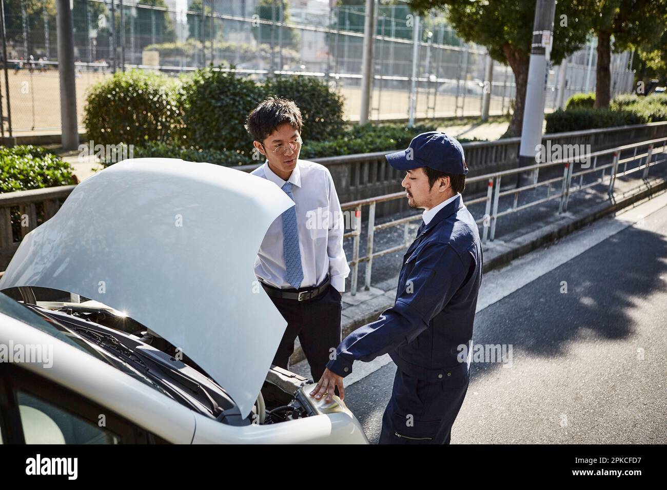 Two men talking in front of car with hood open Stock Photo - Alamy