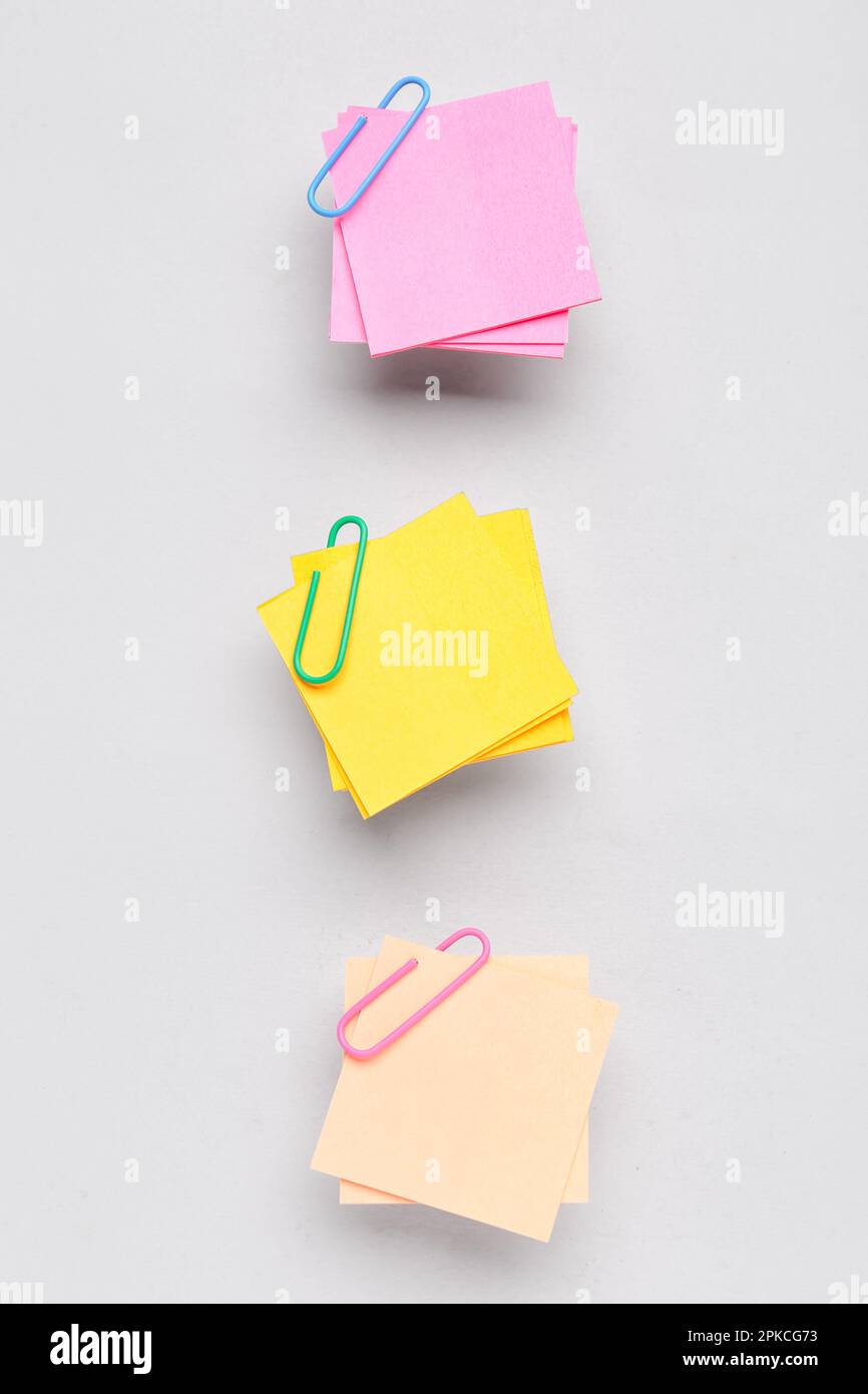 Beige, yellow and pink sticky notes with paper clips on grey background ...