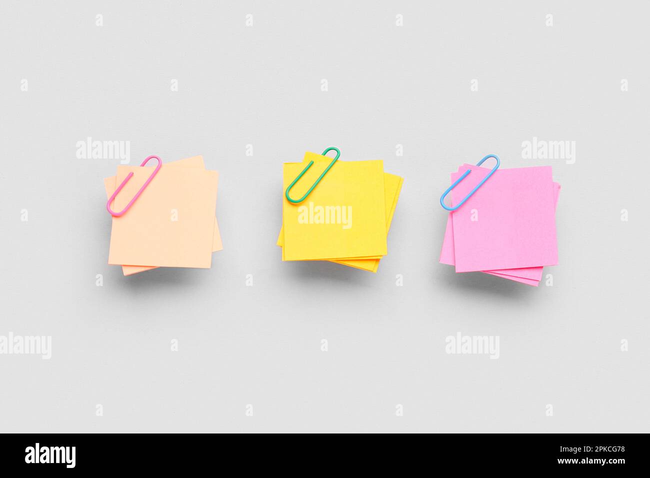Beige, yellow and pink sticky notes with paper clips on grey background ...