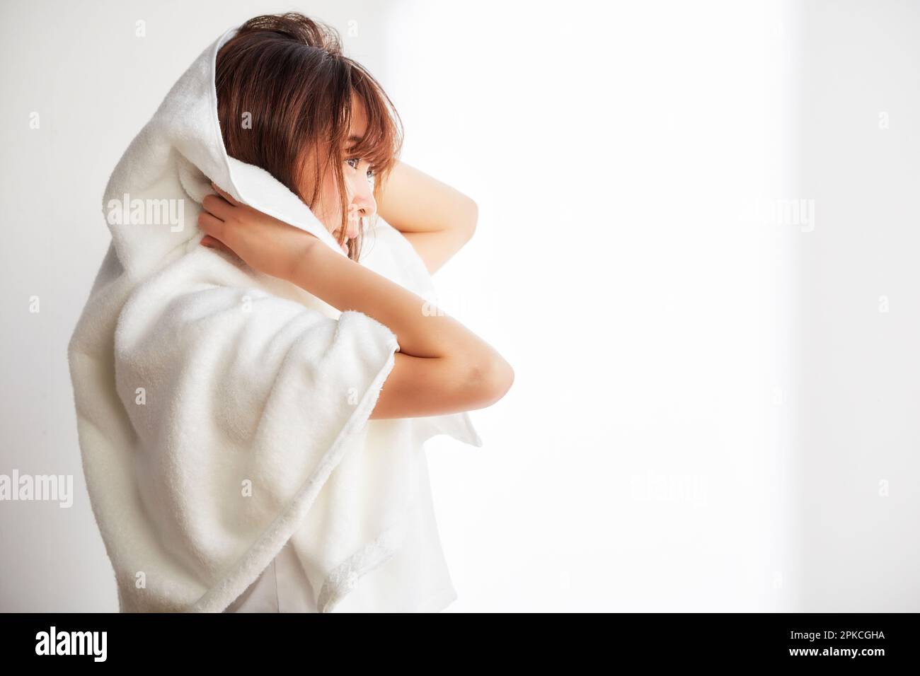Woman wiping her head with white bath towel in front of white wall ...