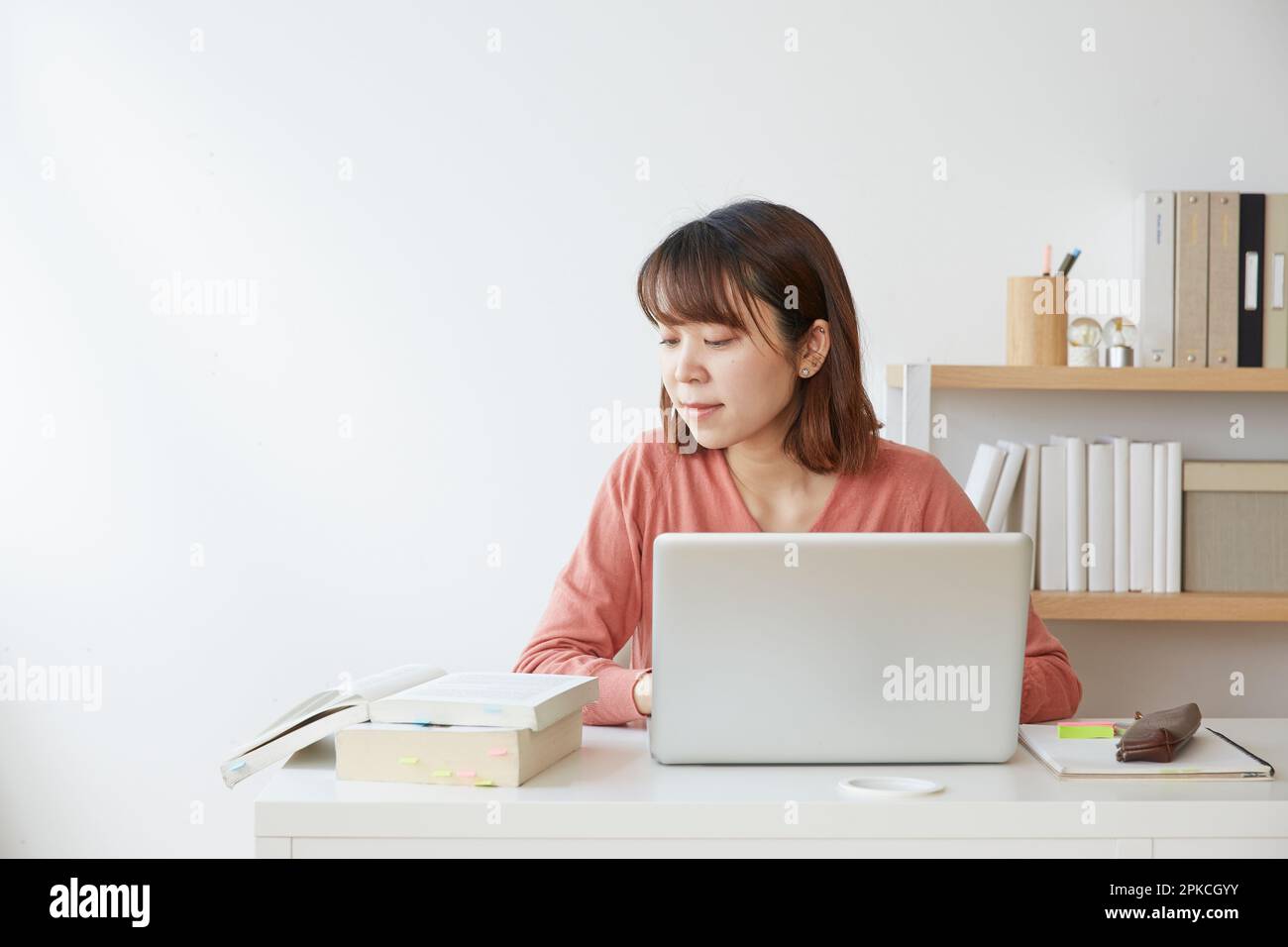 A woman studying on a computer while looking at a reference book Stock ...