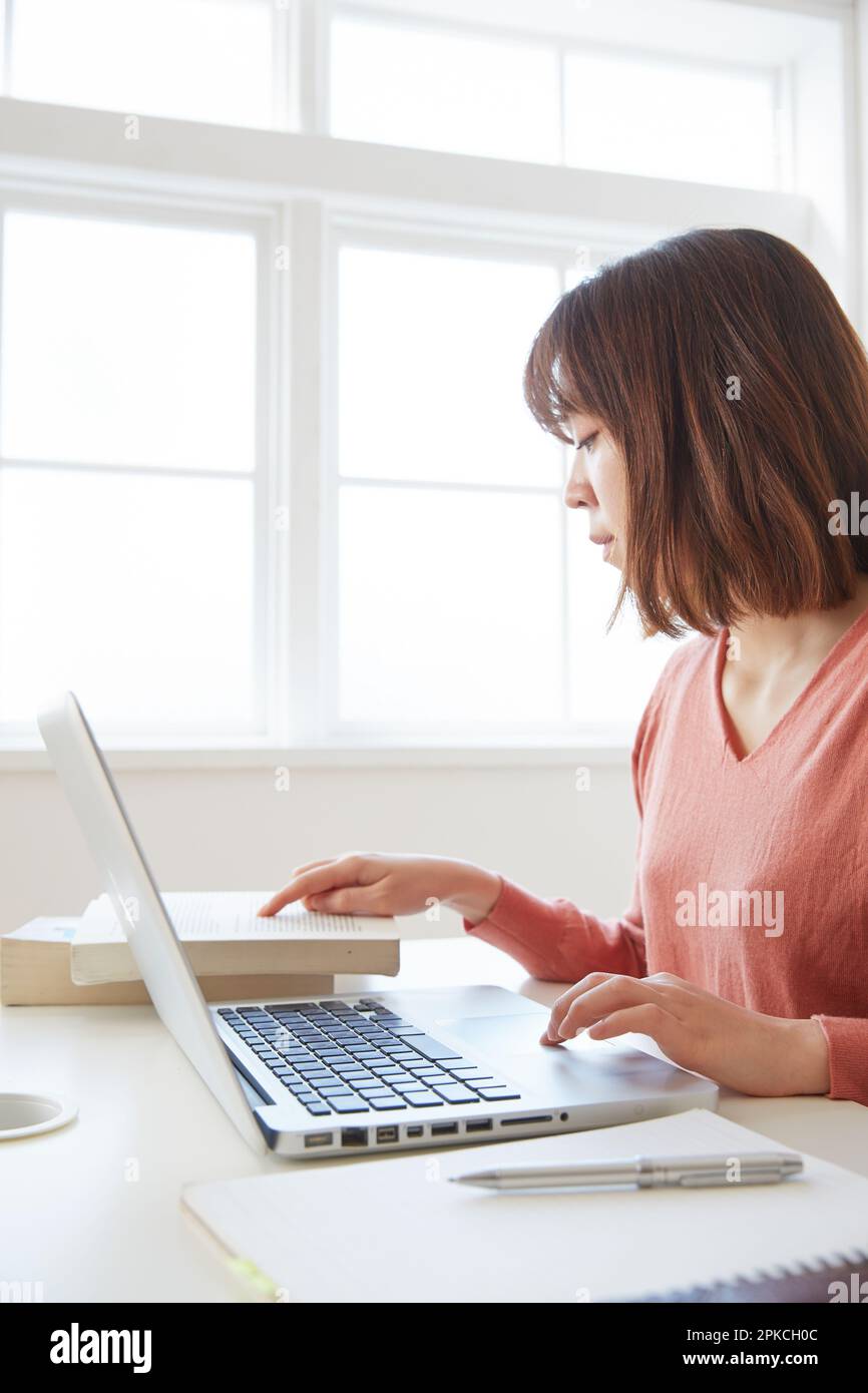 A woman studying on a computer while looking at a reference book Stock ...