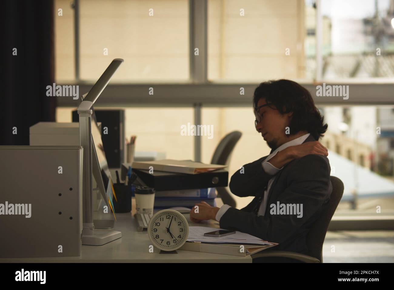 Man rubbing his shoulders at his desk after hours Stock Photo - Alamy