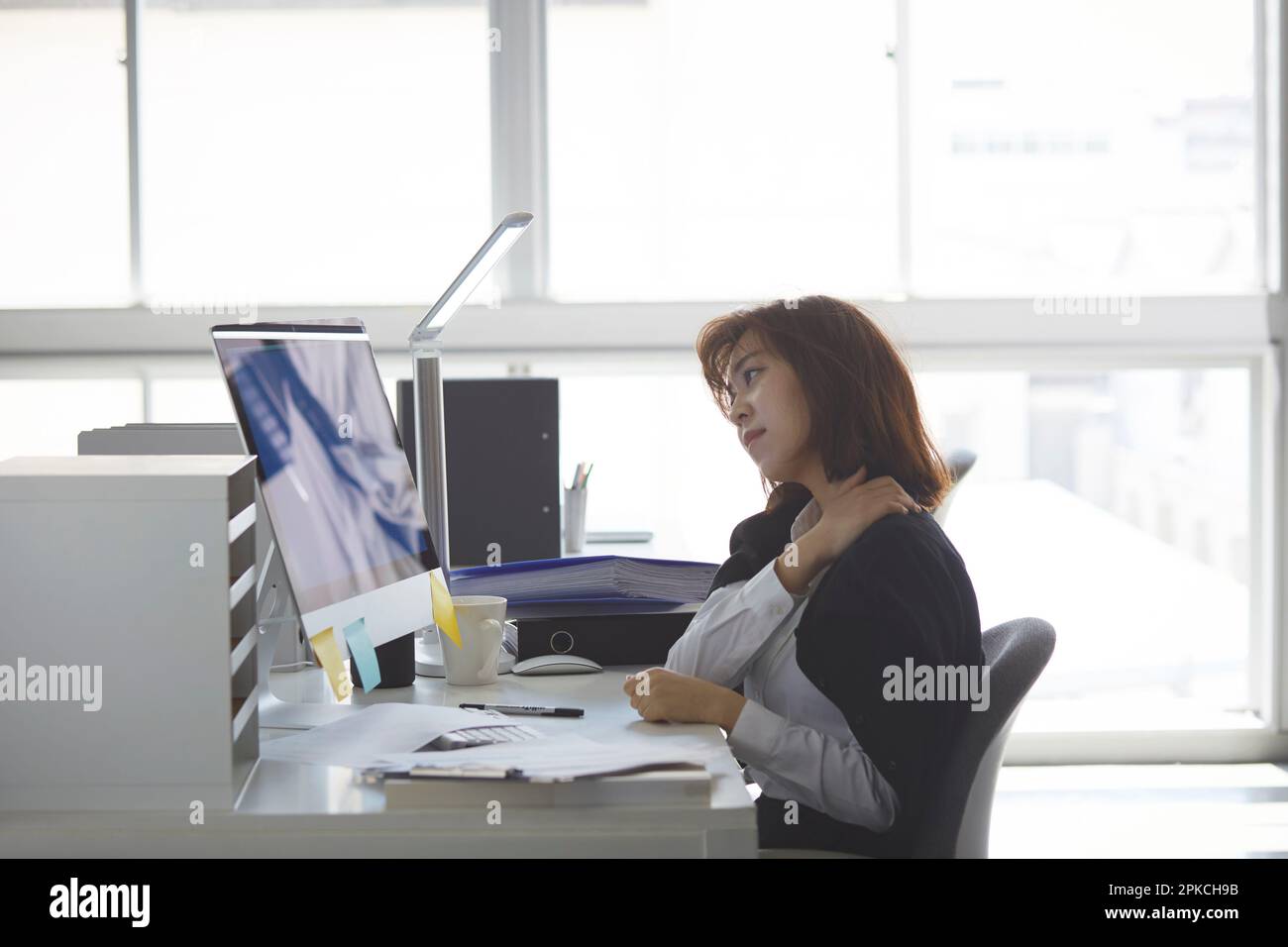 Woman rubbing her shoulders at her desk after staying up all night ...