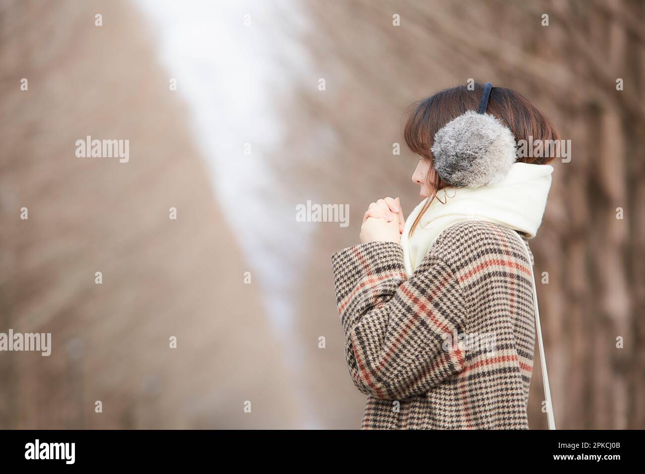 Woman looking cold on a road lined with dead trees Stock Photo - Alamy