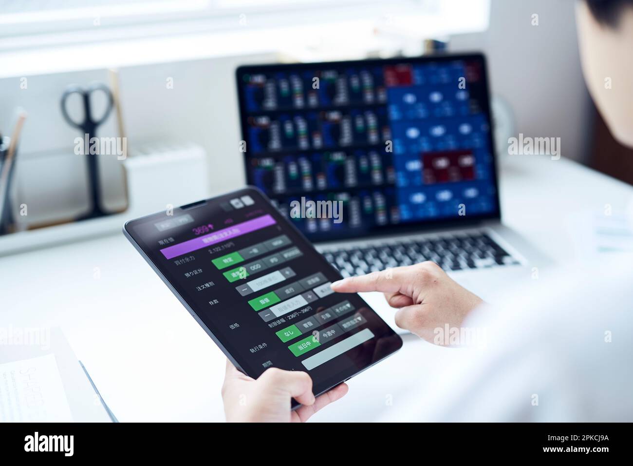 A man placing a stock order with his tablet while checking his computer ...