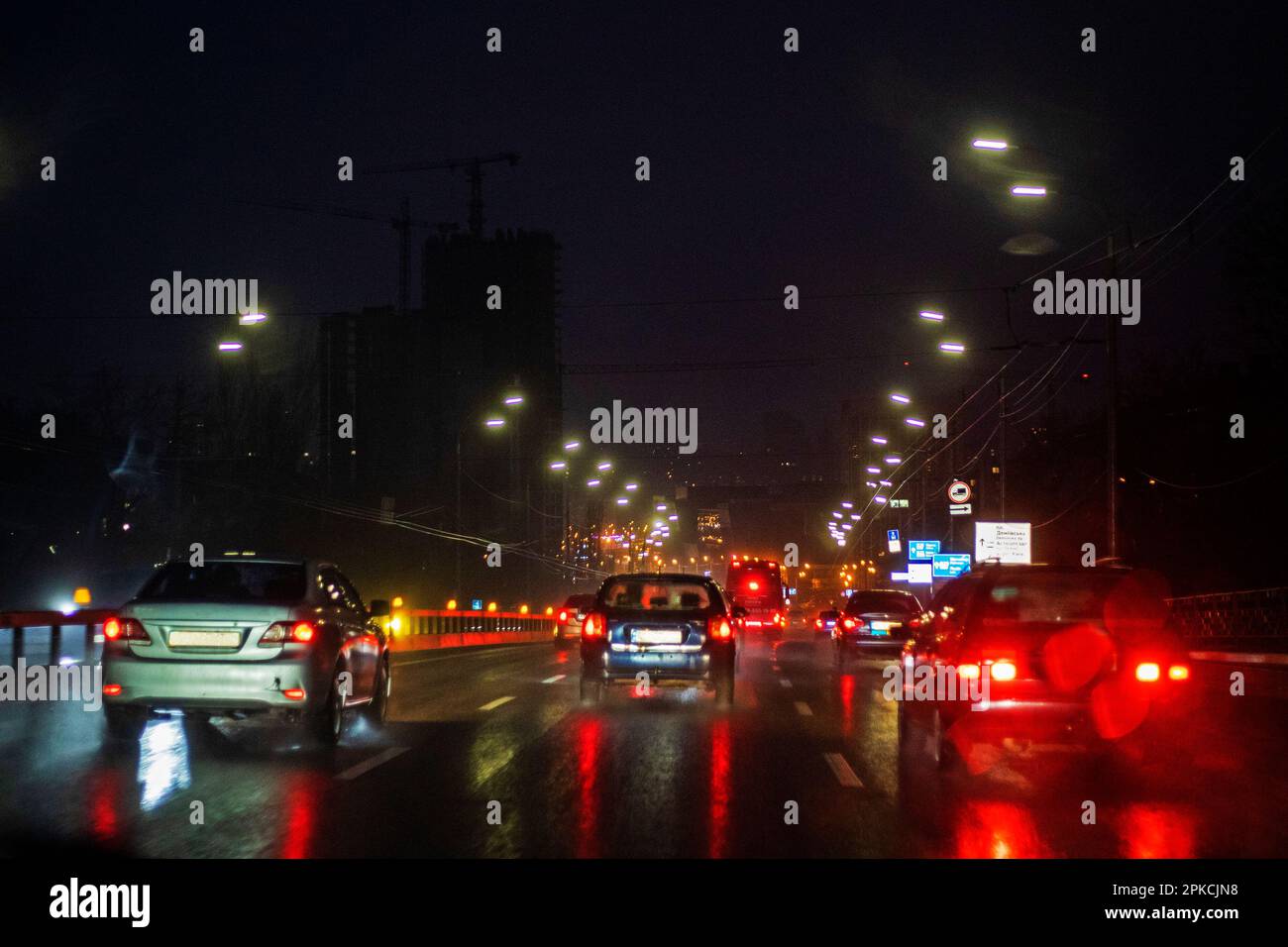 night wet highway in the city illuminated by the red stops of the car ...