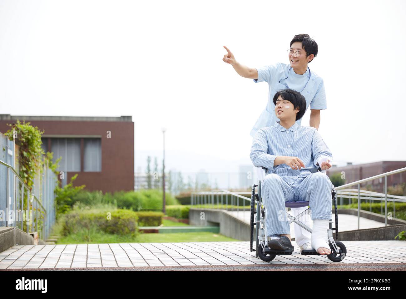 Patient in wheelchair and nurse walking Stock Photo - Alamy