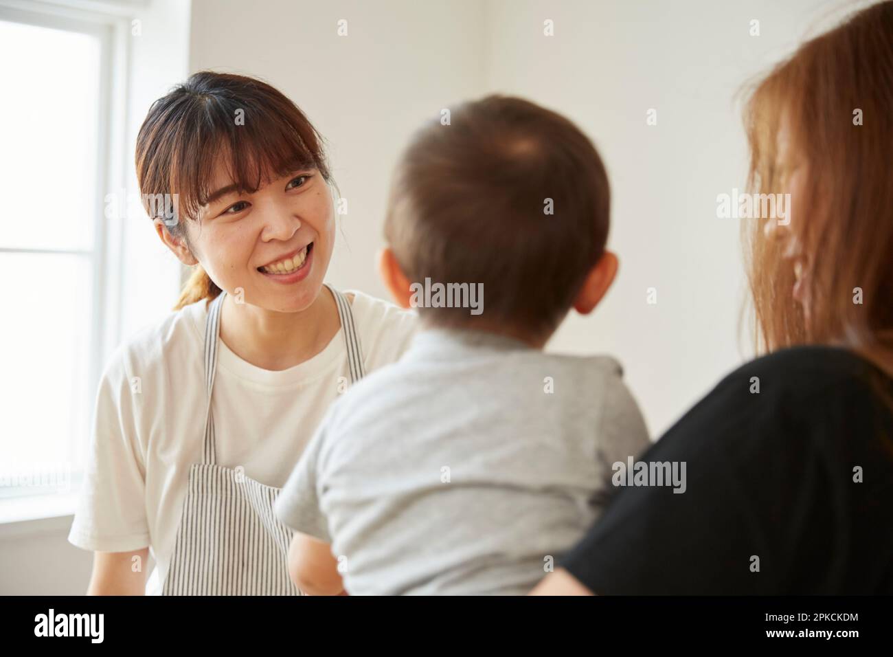 Child care worker smiling at a child being held by his mother Stock ...