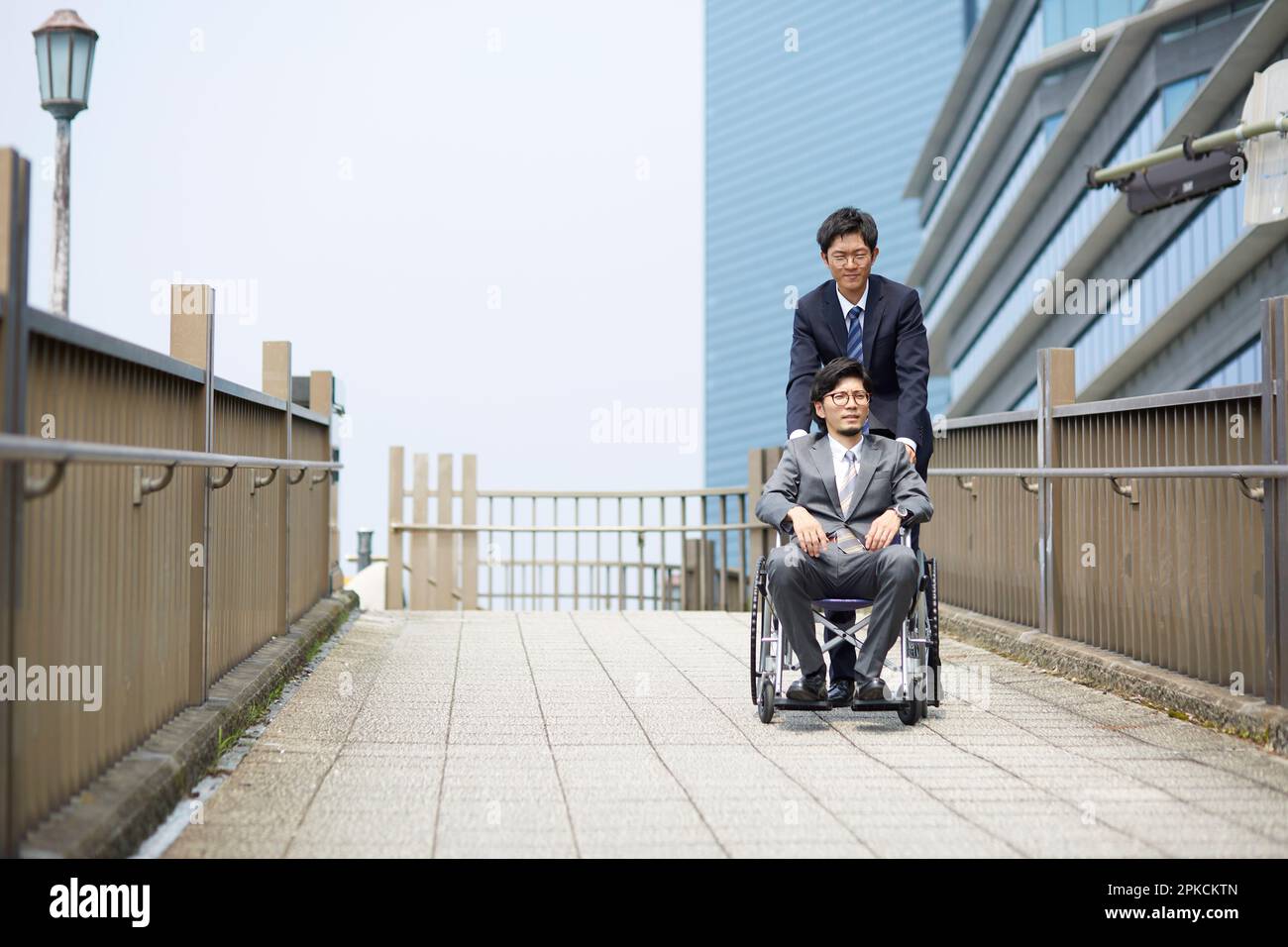 Man in suit pushing man in wheelchair Stock Photo - Alamy