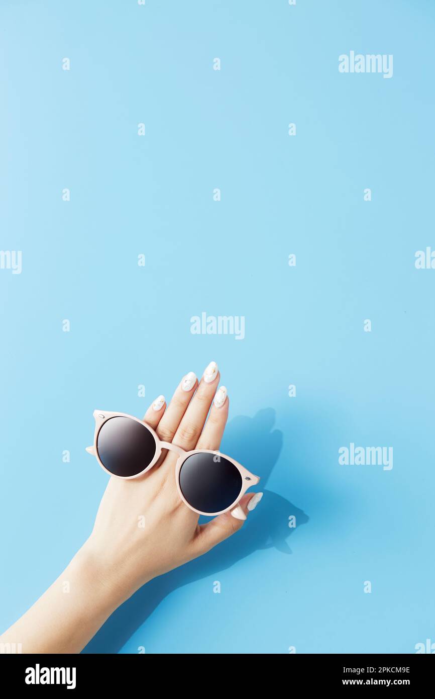 Woman's hand with sunglasses on the back of her hand on light blue ...