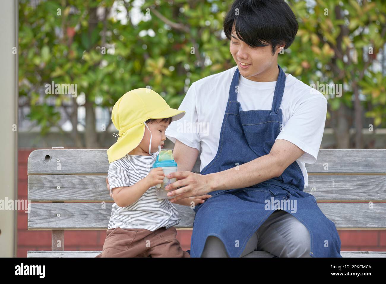 Male child care worker sitting on a bench and giving a cup of tea to a ...