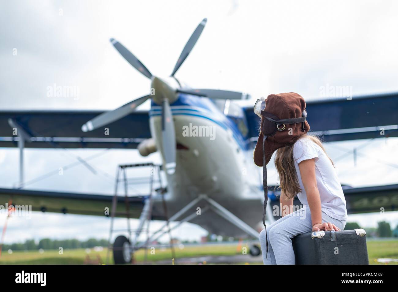 A little girl in a pilot's costume sits on a suitcase against the ...