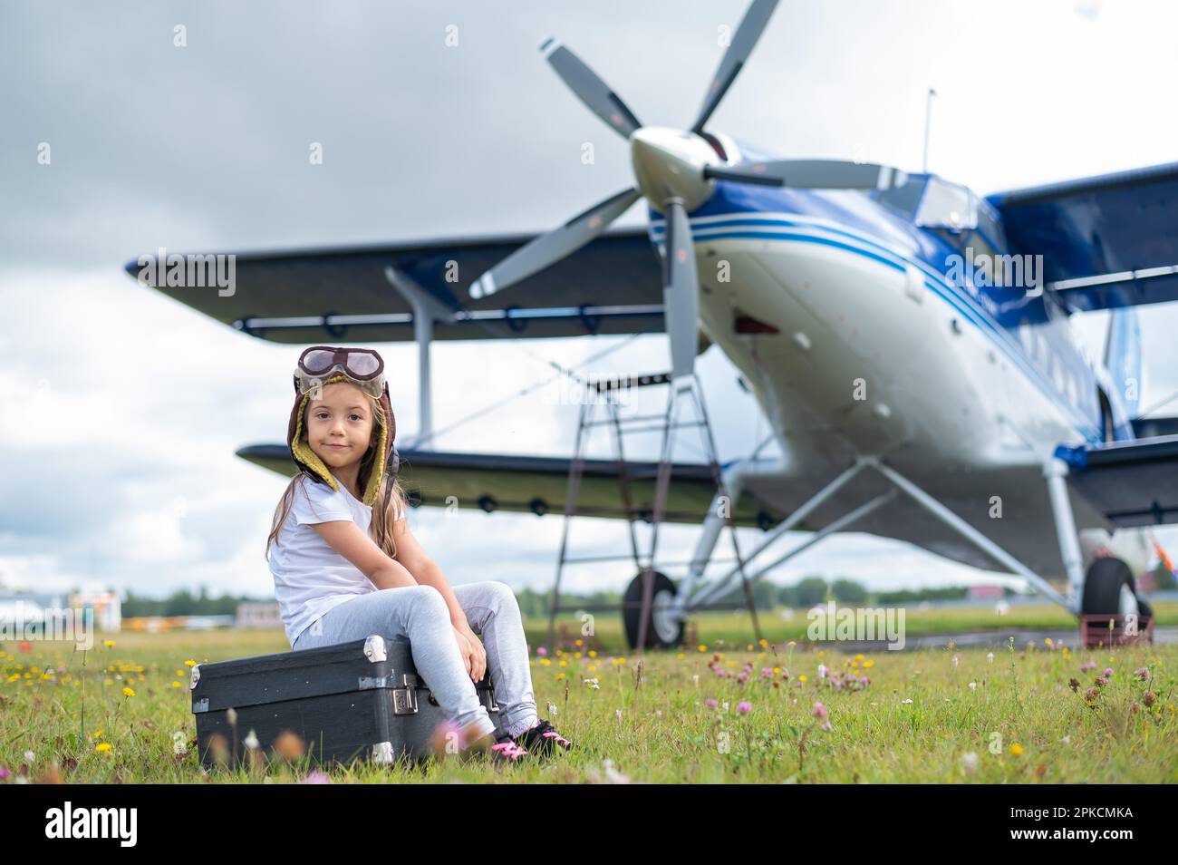 A little girl in a pilot's costume sits on a suitcase against the ...