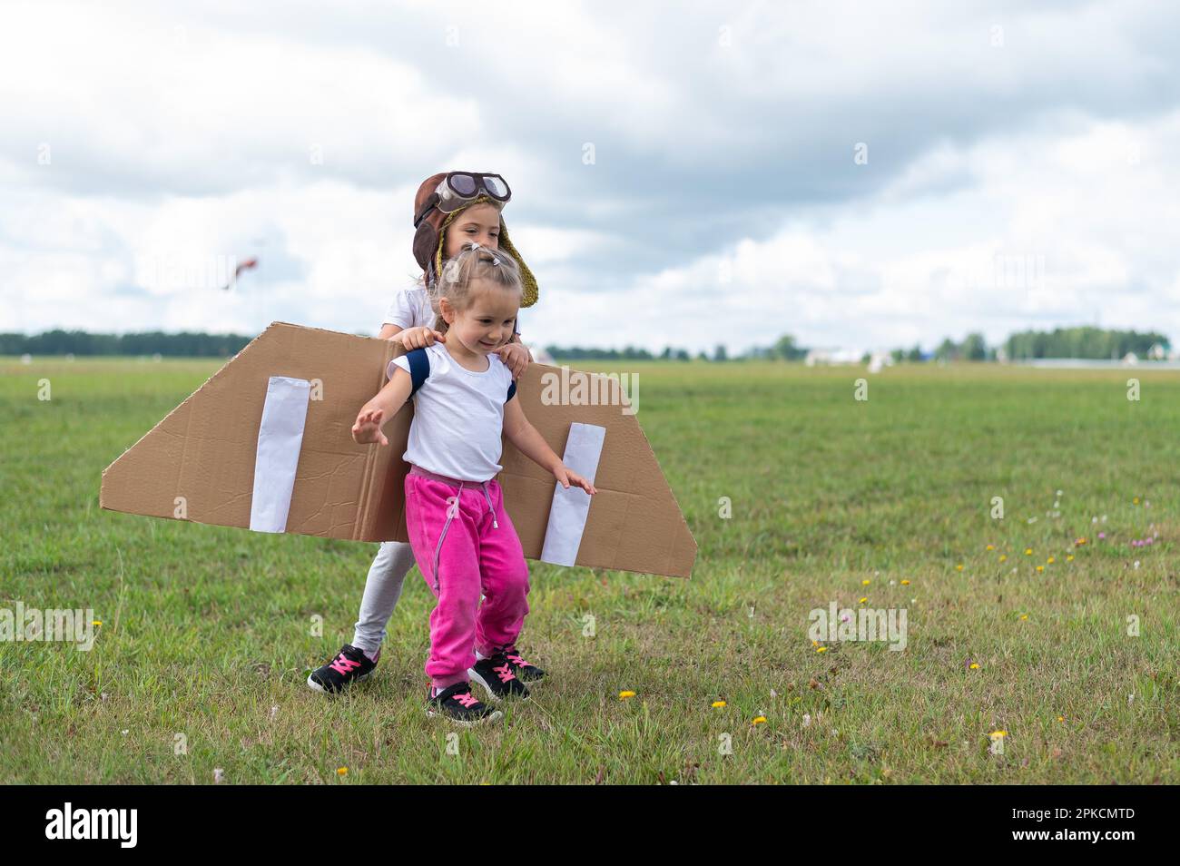 Two little girls in pilot's costumes are hugging in the field. Sisters ...