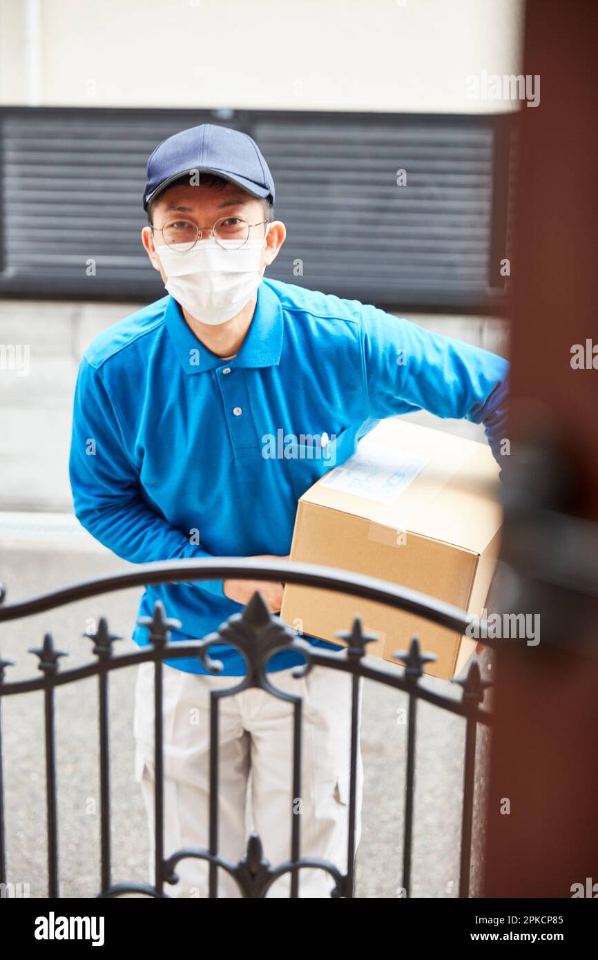 Masked male delivery man greeting behind door Stock Photo - Alamy