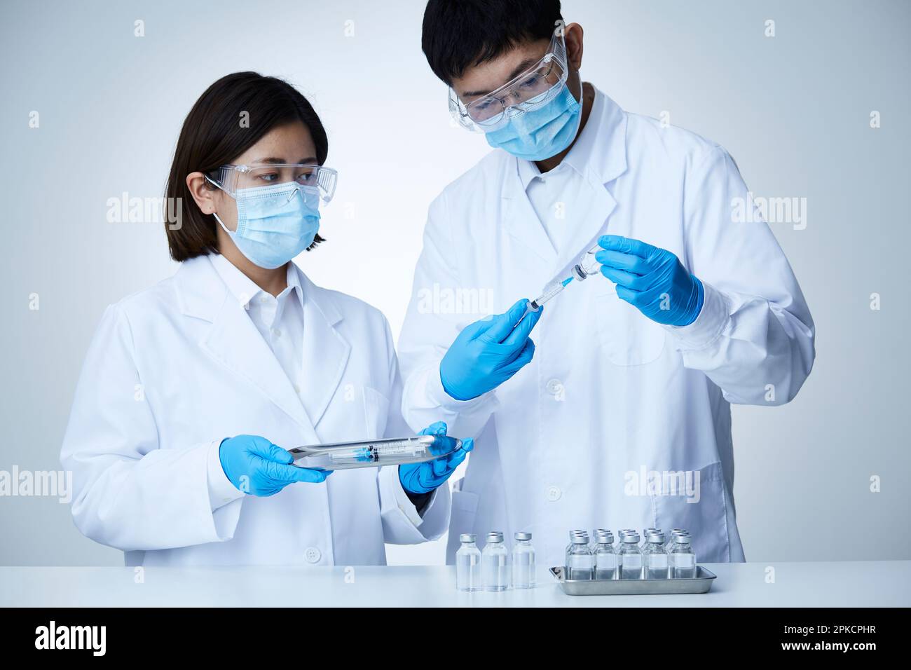 Man and woman in lab coat inserting syringe into bottle Stock Photo - Alamy