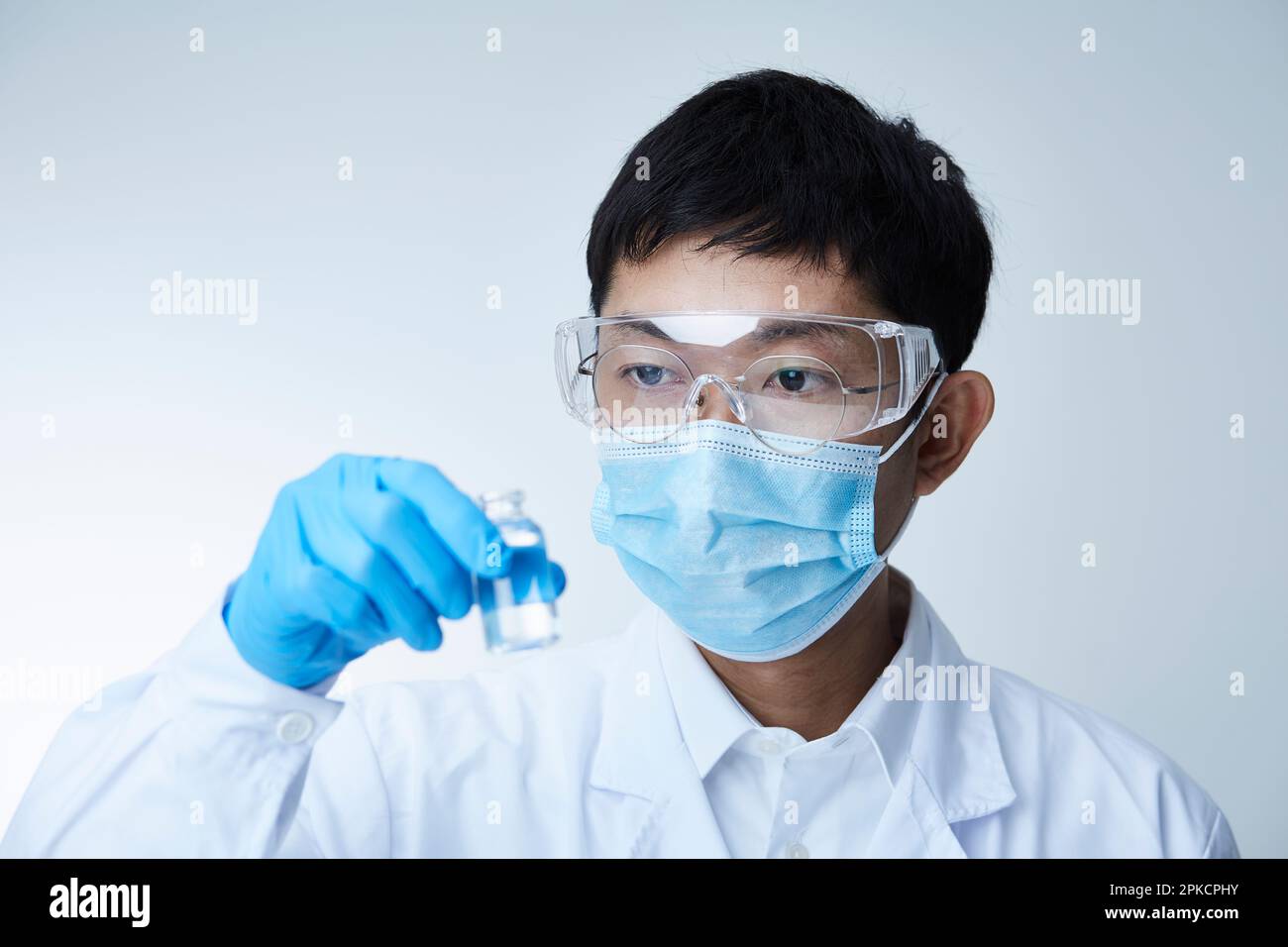 A researcher in a white lab coat looking at a vial Stock Photo - Alamy