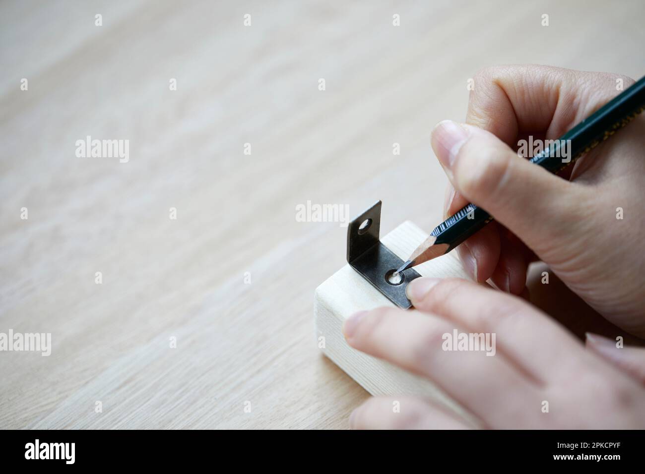 A hand applying an L-shaped bracket to a square piece of wood to mark ...