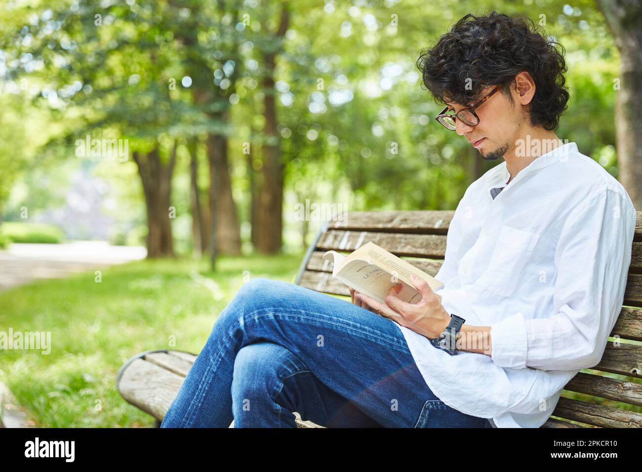 Man reading book sitting on park bench Stock Photo - Alamy