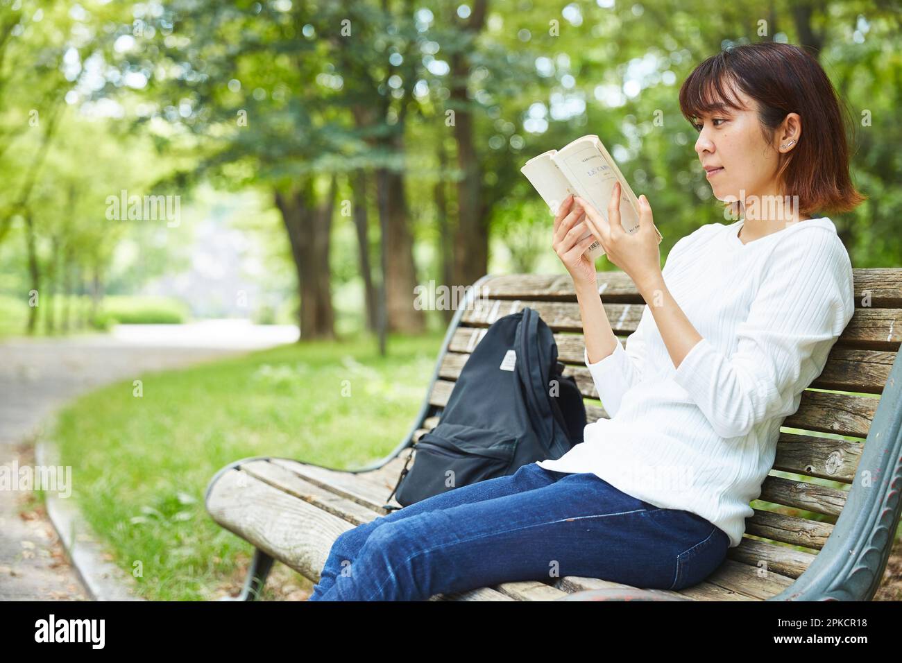 Woman reading a book sitting on a park bench Stock Photo - Alamy