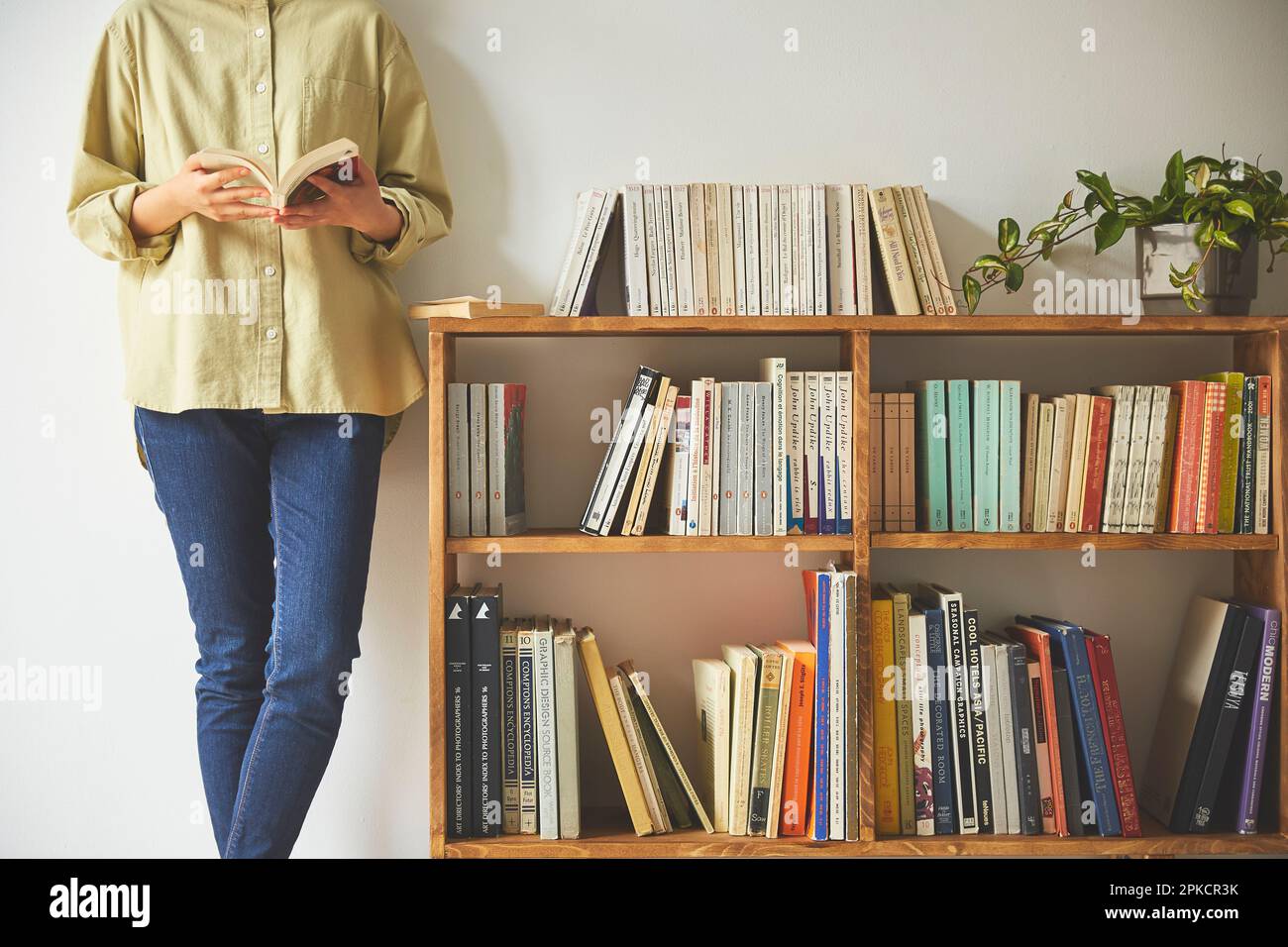 Woman standing next to bookshelf reading book Stock Photo - Alamy