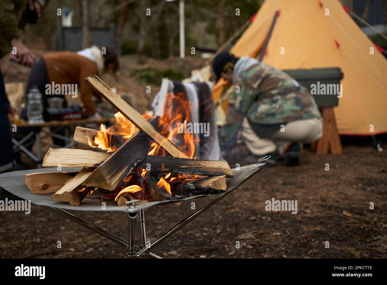 Men and women preparing to cook over a campfire at a winter campsite ...